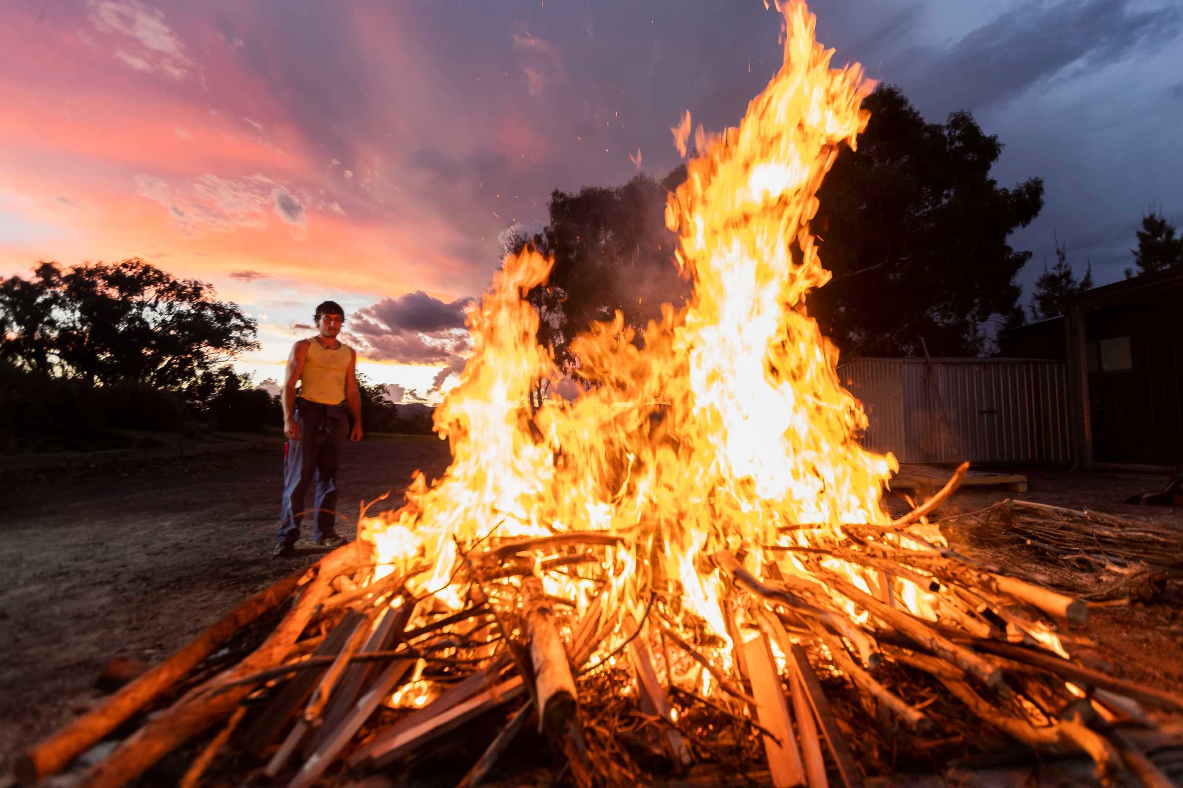 A photograph of a large bonfire with the artist in the background